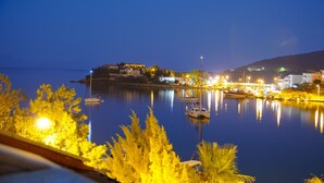 Uma cidade costeira à noite, com águas calmas, barcos e edifícios iluminados.