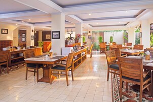 Um restaurante espaçoso com mesas e cadeiras de madeira, área de bar e vista para o verde lá fora.