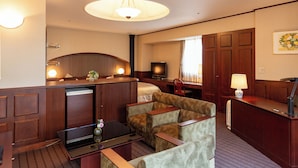 Quarto de hotel com uma cama, uma escrivaninha com computador, televisão e um espaço de estar com cadeiras.