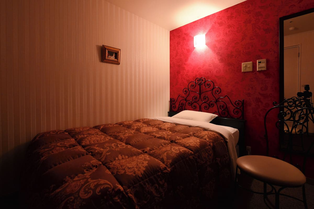 Quarto com cama, uma cadeira, luminária na parede e um espelho.