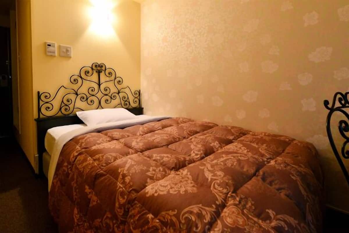 Uma cama com colcha estampada, luminária fixada na parede e papel de parede com padrão floral.