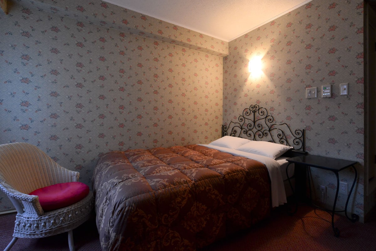 Quarto com cama, cadeira, mesa de cabeceira e luminária na parede.