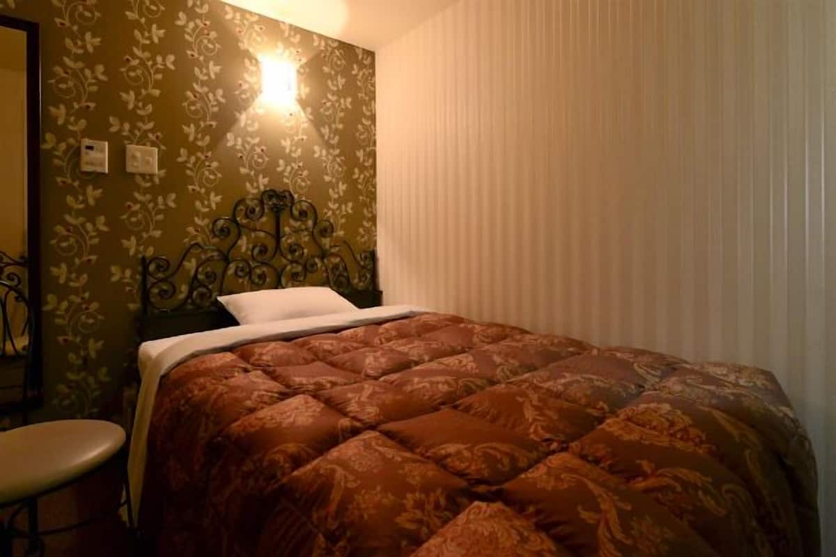 Quarto de hotel com uma cama, uma cadeira, parede com papel de parede floral e luminária.