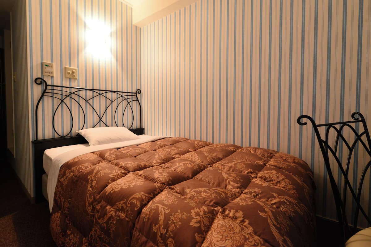 Cama bem arrumada com colcha floral marrom em um quarto com papel de parede listrado.