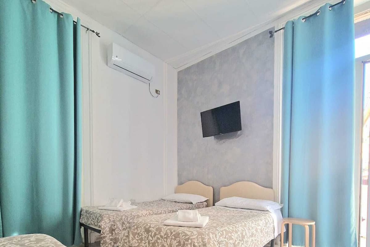 Quarto de hotel com duas camas, televisão na parede e janela com cortinas.