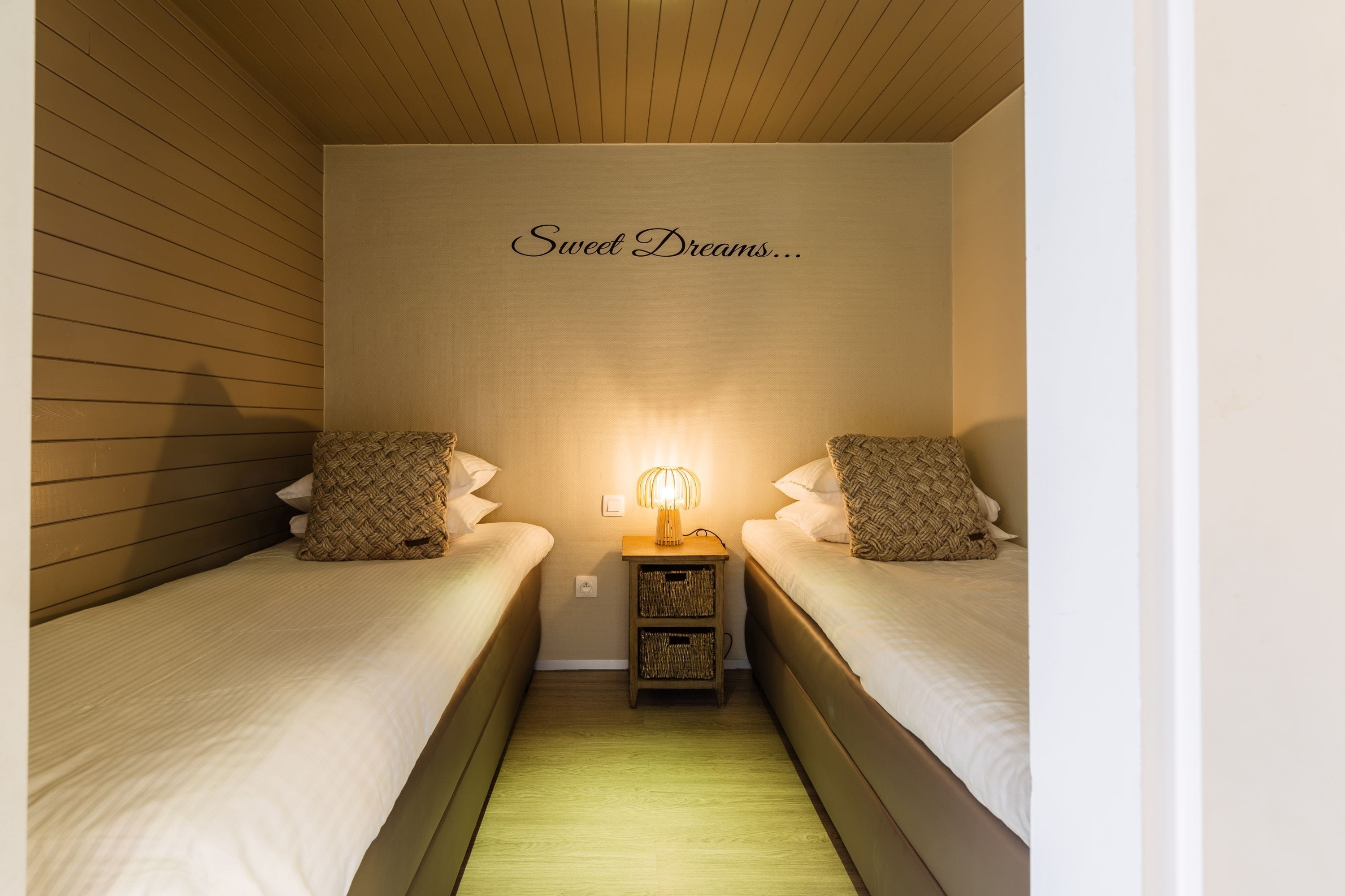 Quarto com duas camas, uma mesa de cabeceira com abajur e parede com a inscrição 'Sweet Dreams...'.