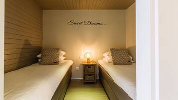 Quarto com duas camas, uma mesa de cabeceira com abajur e parede com a inscrição 'Sweet Dreams...'.