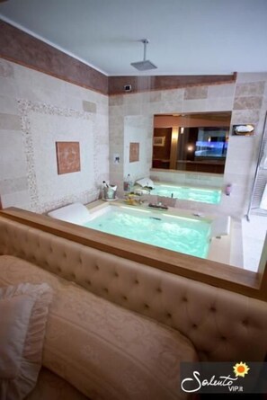 Um quarto com uma banheira grande, um sofá e um espelho refletindo o ambiente.
