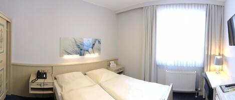 Quarto de hotel com cama, mesa de cabeceira, luminária e um quadro na parede.
