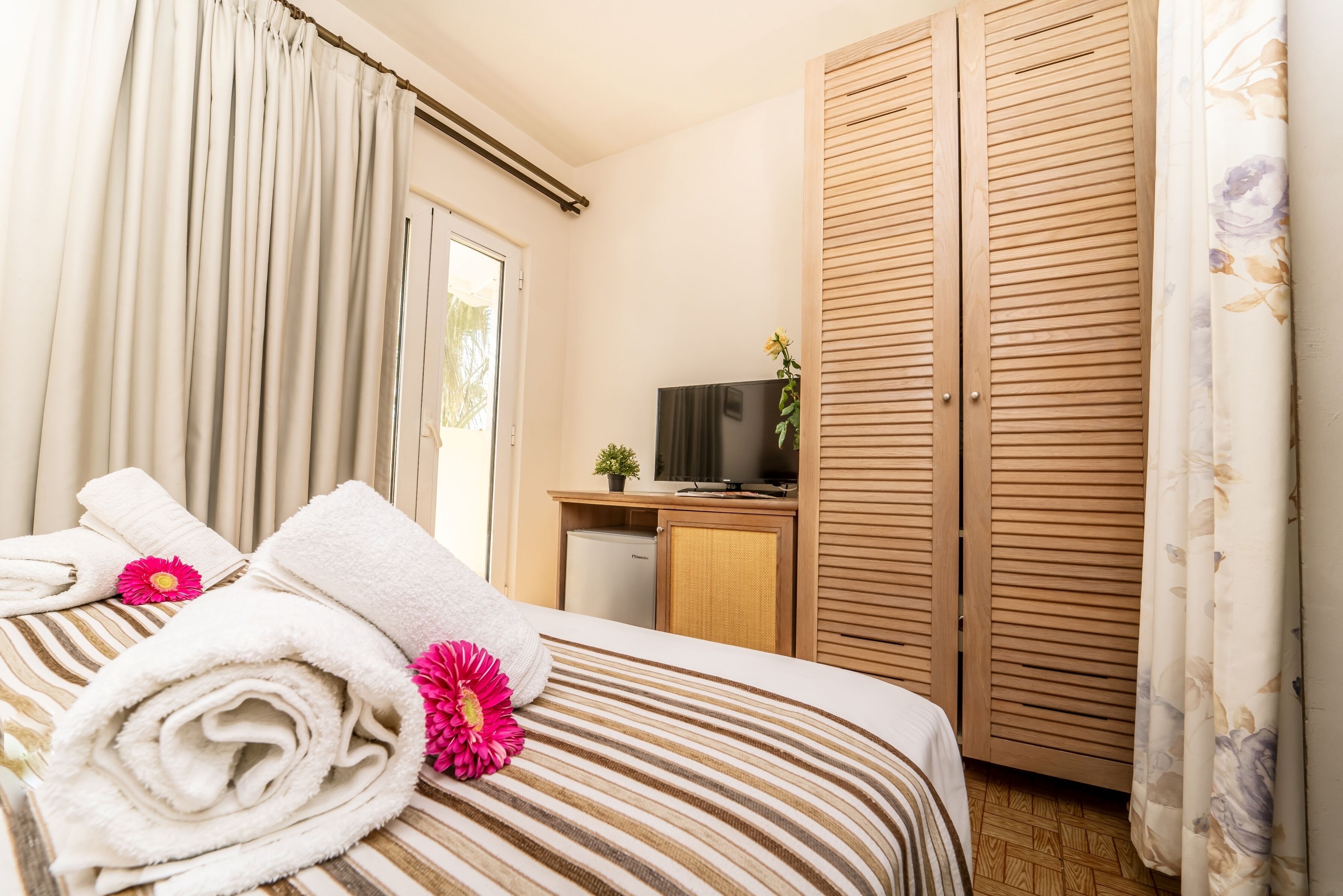 Quarto de hotel com cama, escrivaninha, televisão e guarda-roupa.
