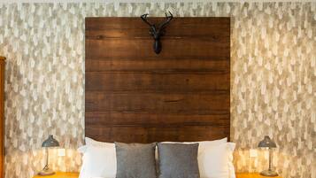 Quarto com cabeceira de madeira, duas luminárias de apoio e cama com almofadas brancas e cinzas.