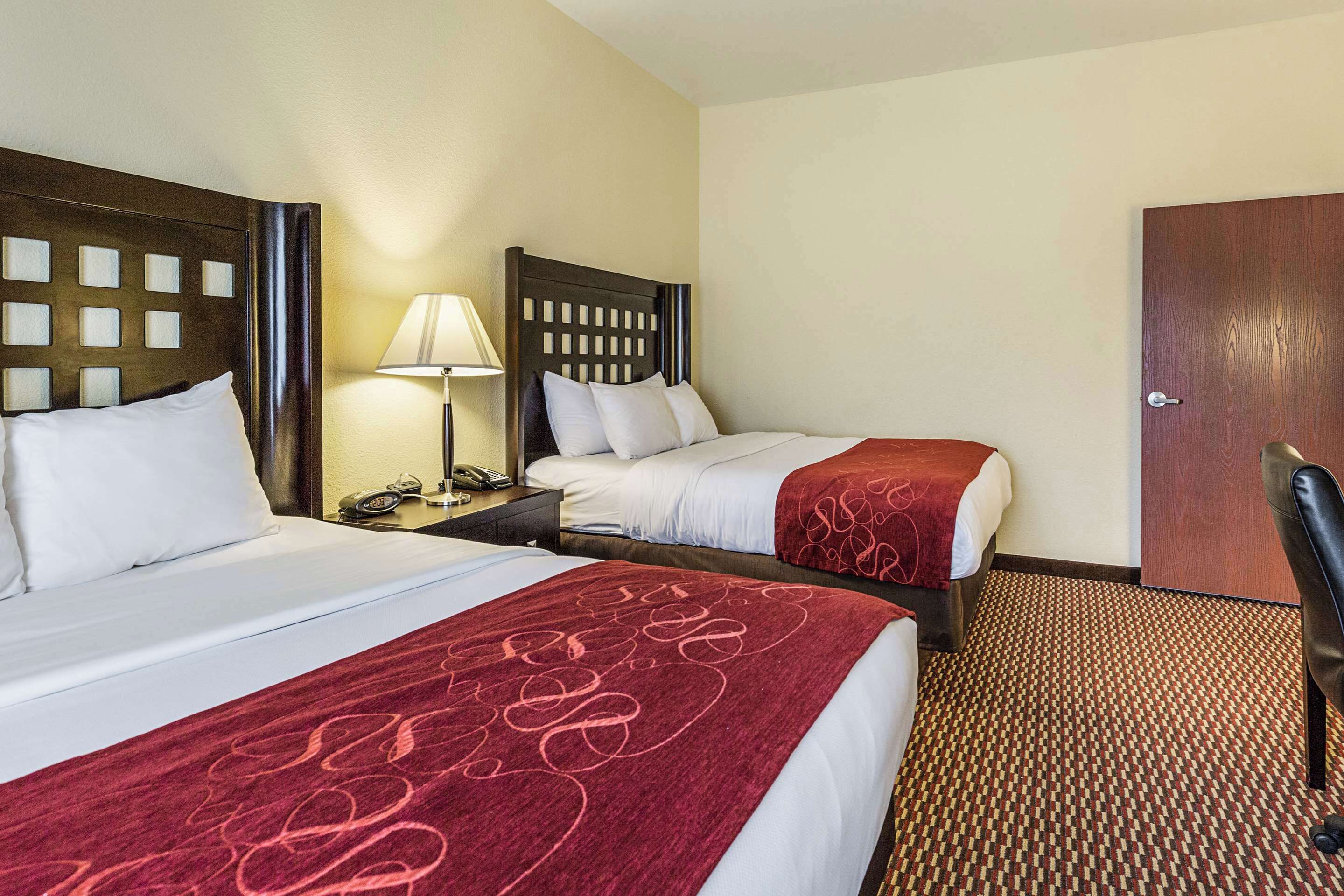 Quarto de hotel com duas camas, uma mesa com abajur e uma porta.
