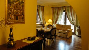 Uma área de refeições com mesa, cadeiras e um vaso. Há um quadro na parede e uma janela com cortinas.