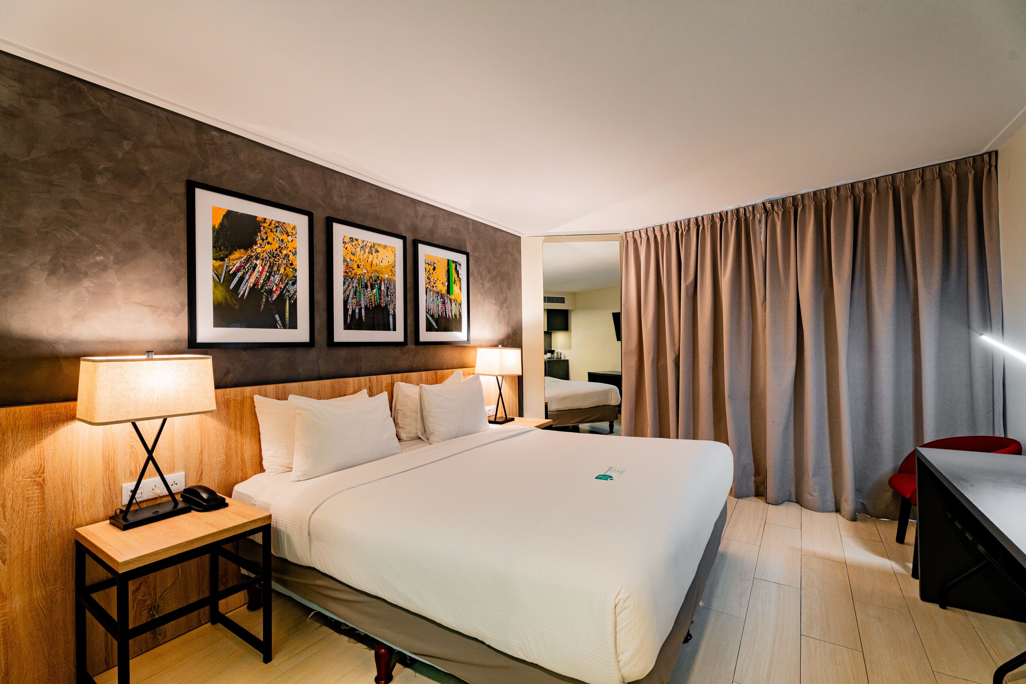 Quarto de hotel com uma cama grande, duas mesas de cabeceira com luminárias, uma escrivaninha e uma cadeira.