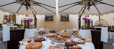 Mesa de buffet com diversos doces e pâtisseries sob guarda-sóis brancos.