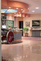 Uma área de recepção de hotel com um balcão curvo, uma televisão, um computador e um vaso de planta.