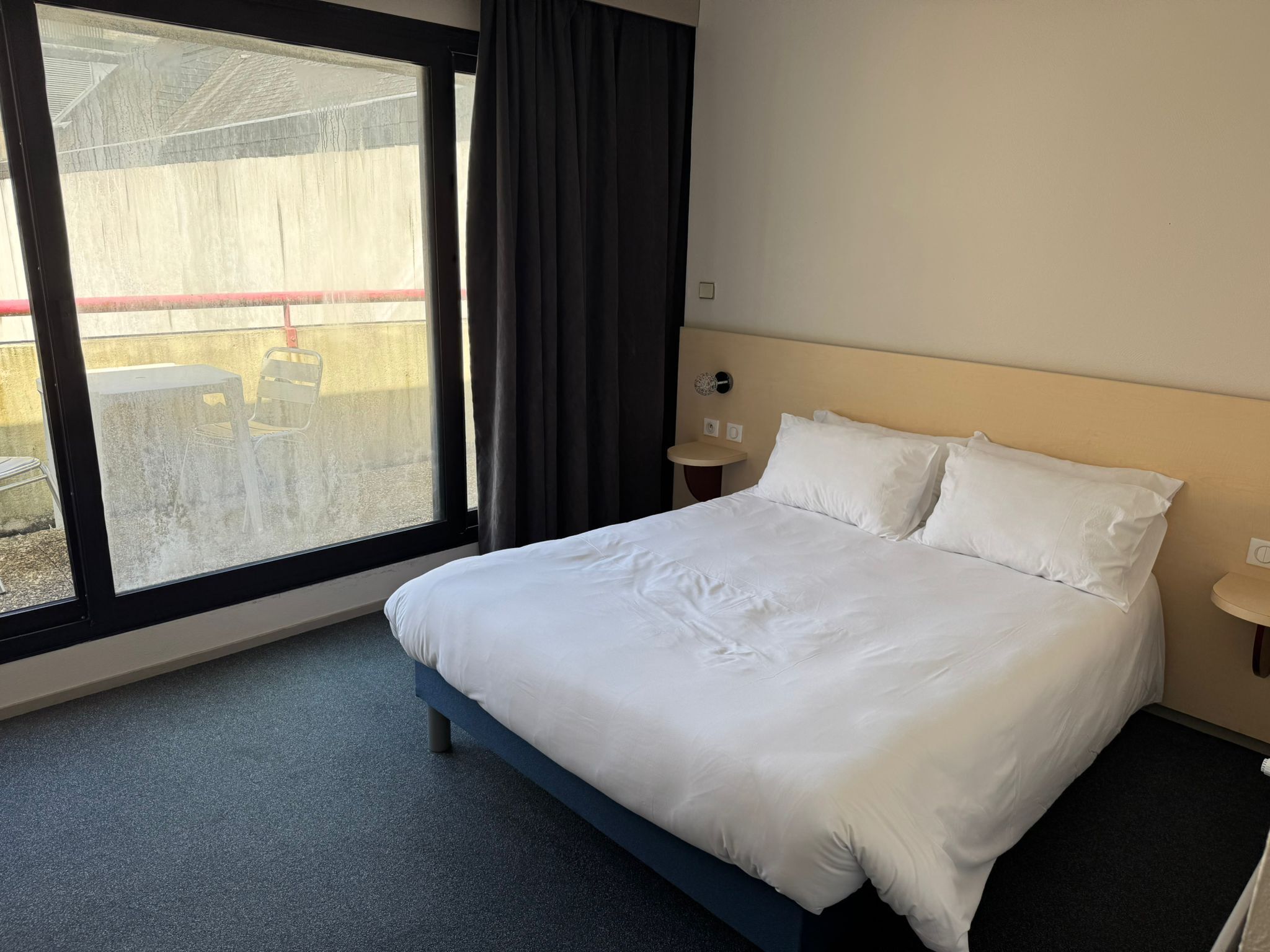 Quarto de hotel com uma cama grande, uma janela com cortinas, uma mesa de cabeceira pequena e vista para o exterior.