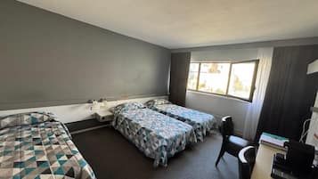 Quarto de hotel com duas camas, uma escrivaninha, uma cadeira e uma janela com cortinas.