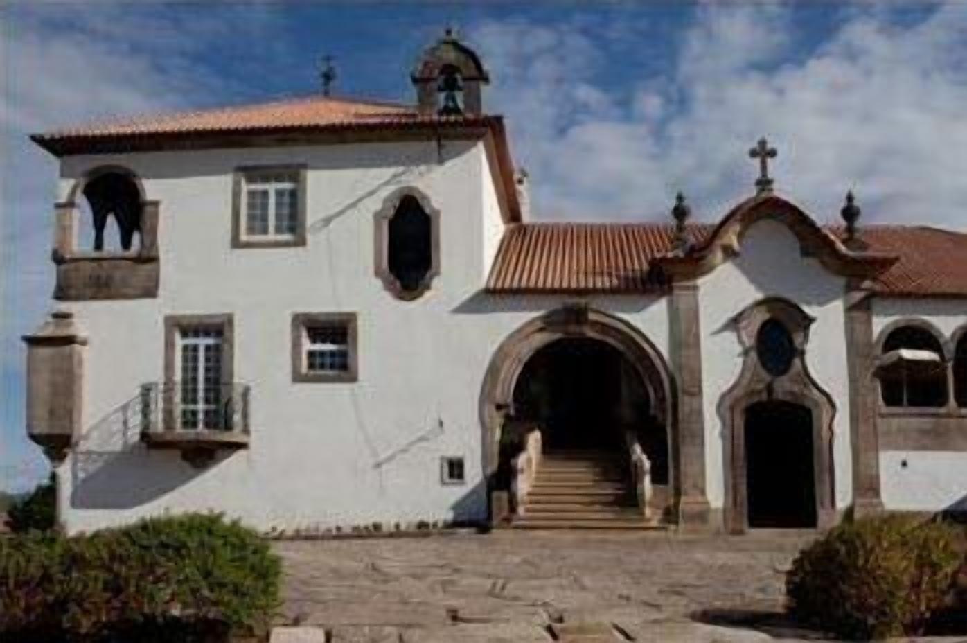 Um edifício branco com telhado de telhas vermelhas, um arco central e uma torre de sino.