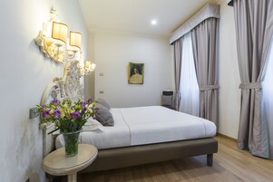 Quarto com cama, mesa de cabeceira, luminária na parede e um vaso com flores.
