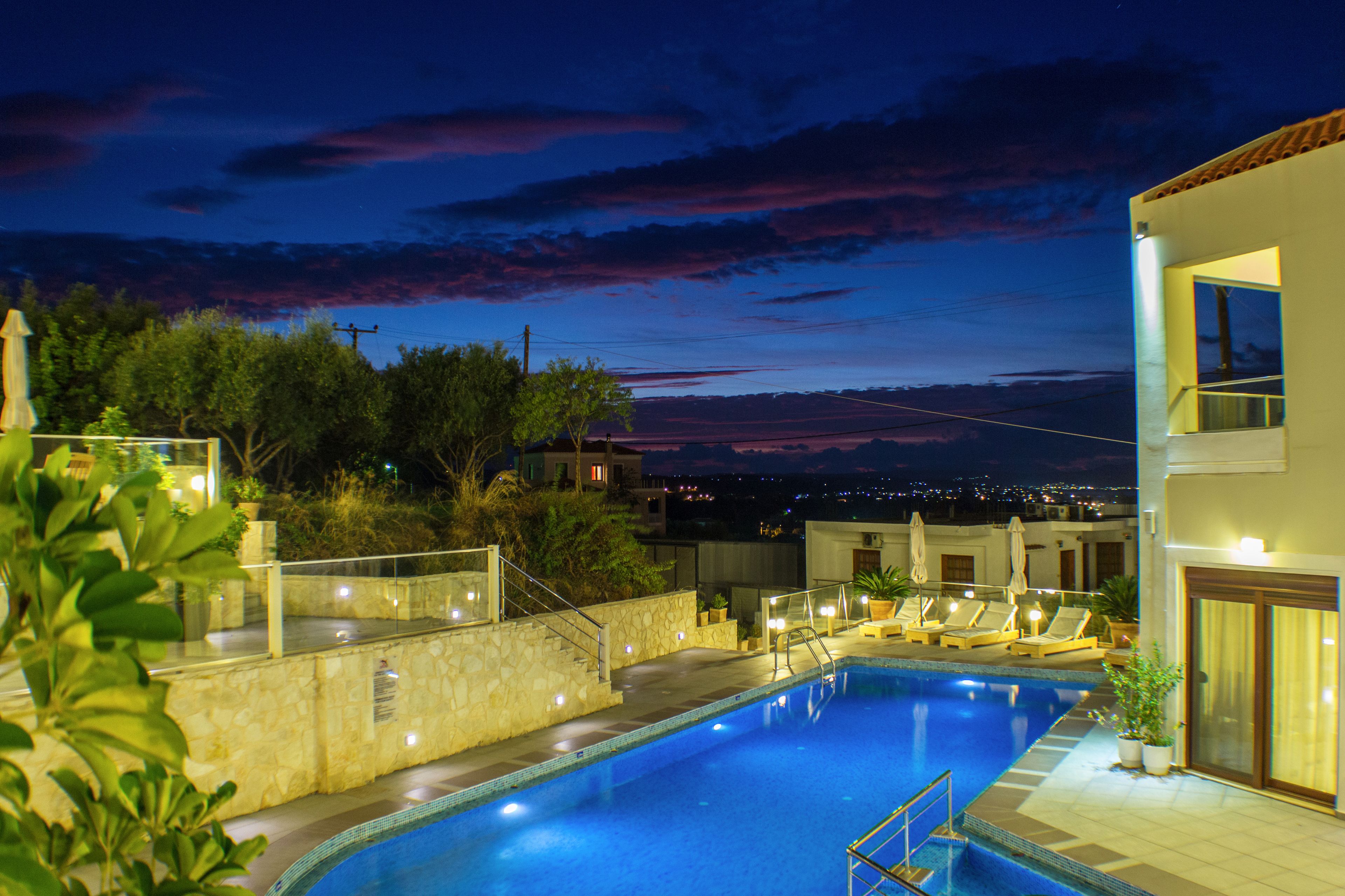 Piscina com espreguiçadeiras e vista da cidade ao entardecer.