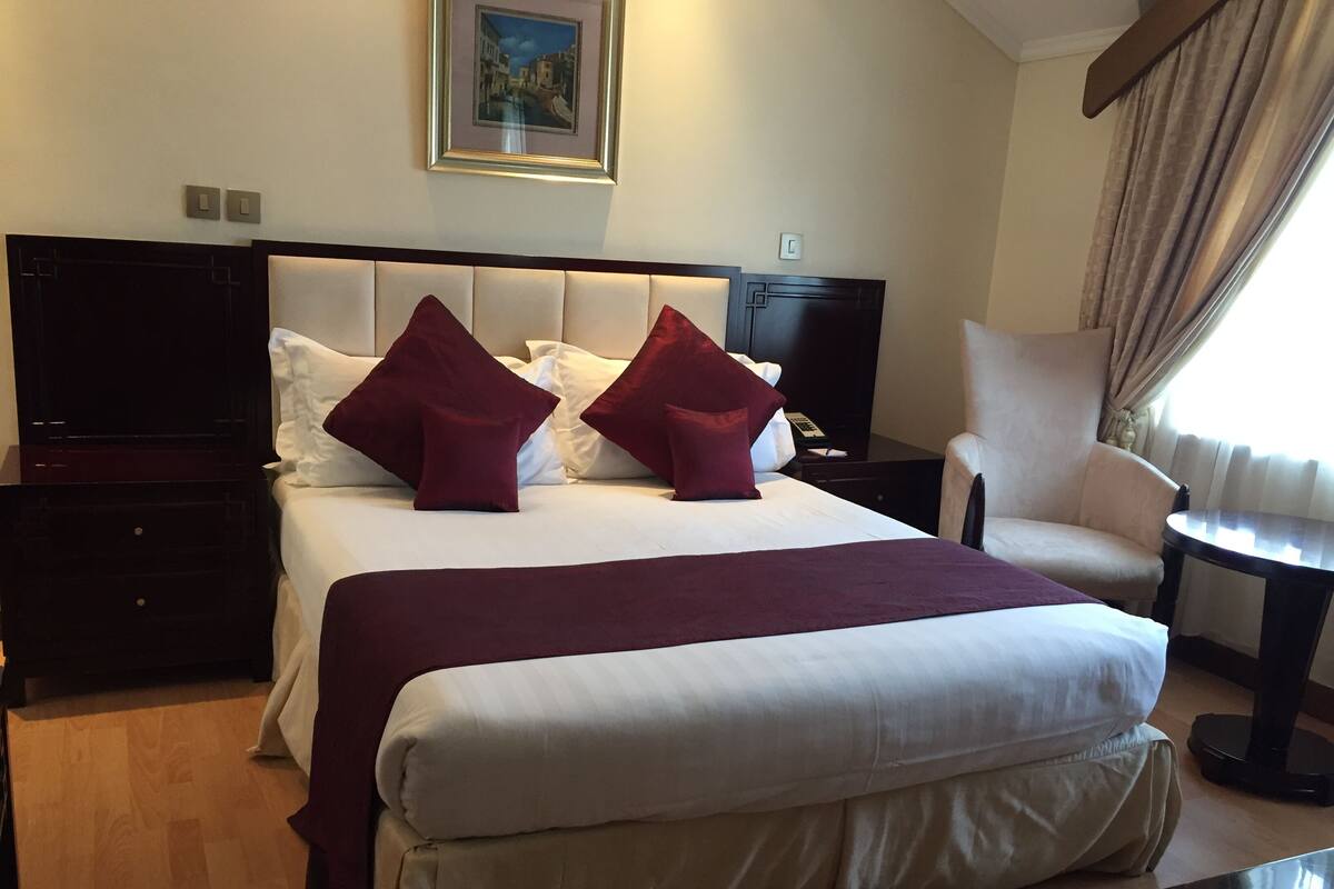 Quarto de hotel com uma cama grande, uma escrivaninha, uma cadeira, uma televisão e um quadro na parede.