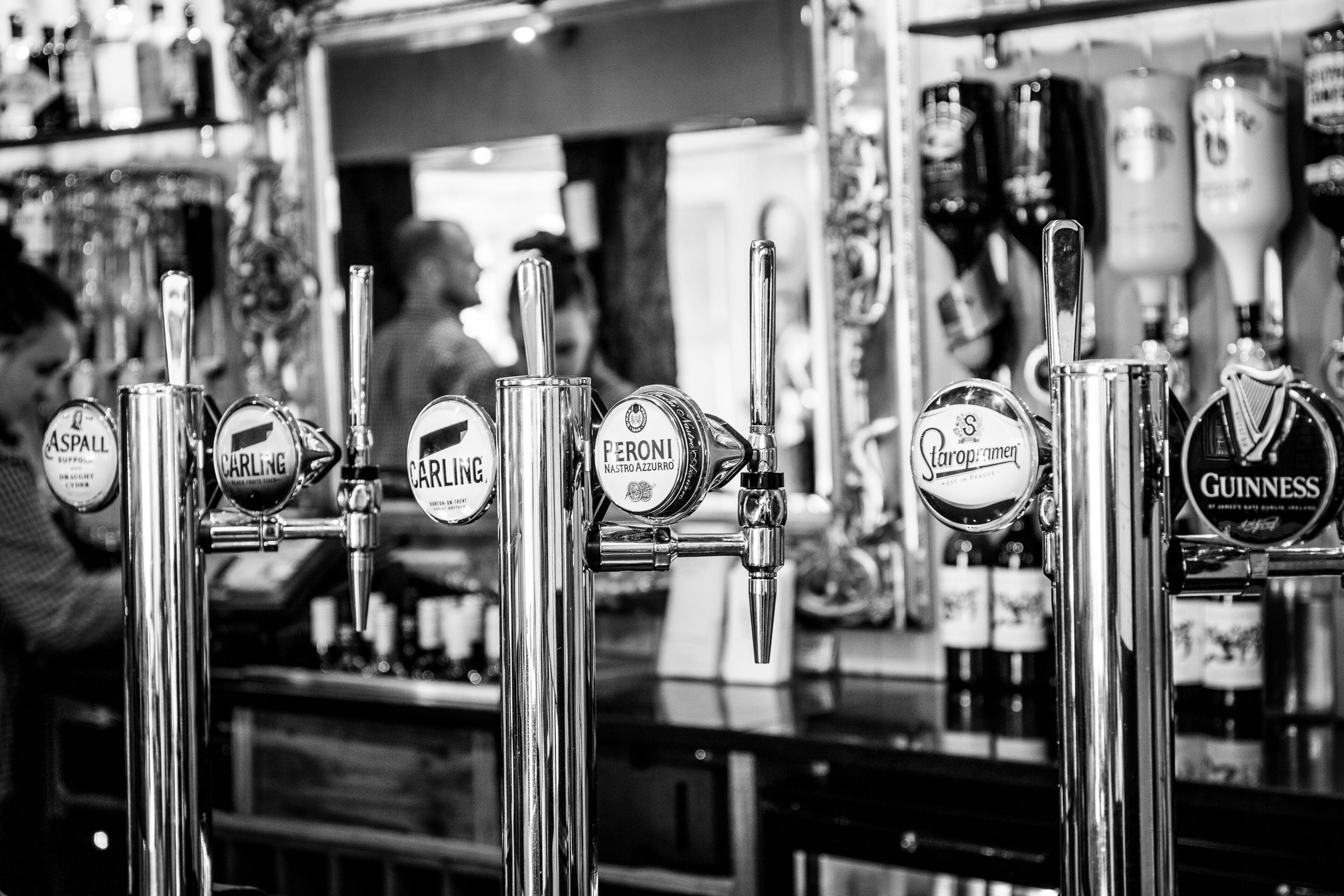 Um balcão de bar com diversas torneiras de cerveja, incluindo marcas como Carling, Peroni e Guinness.