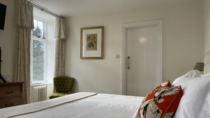 Quarto com cama, cadeira, radiador, porta e um quadro na parede.