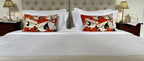 Cama bem arrumada com roupa de cama branca, duas almofadas decorativas com padrão de pássaros, cabeceira estofada e luminárias nas mesas de cabeceira de madeira.