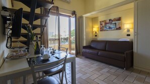 Uma área de refeições com uma mesa posta para dois, um sofá de couro marrom e uma varanda com vista.