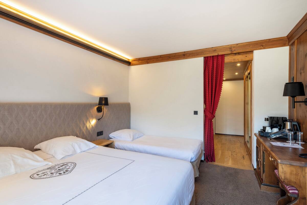 Quarto de hotel com duas camas, uma escrivaninha com abajur e cortina vermelha.