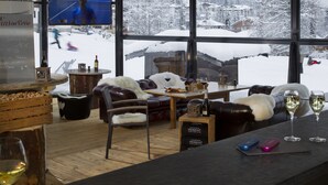 Ambiente acolhedor com área de bar, assentos de couro e uma janela ampla com vista para a neve.