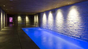 Área interna de piscina moderna com um recurso aquático iluminado em azul, teto de madeira e paredes de pedra.