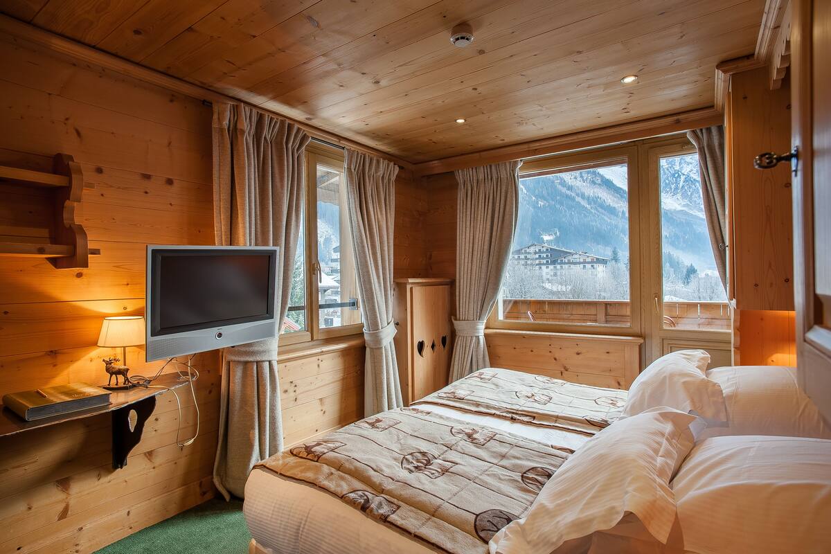 Quarto de cabana de madeira com uma cama, uma TV e vista para montanhas.