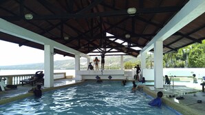 Piscina interna com cobertura e vista para a paisagem, com pessoas praticando diversas atividades.