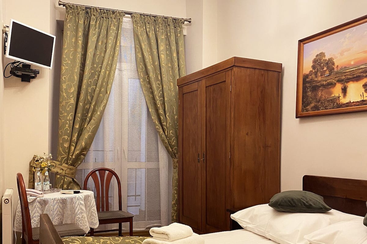 Quarto com cama, guarda-roupa de madeira, escrivaninha com computador e um quadro na parede.