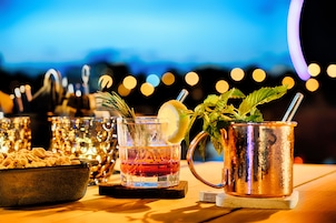 Uma mesa com diversas bebidas, incluindo um cocktail com rodela de limão e hortelã, e uma caneca de cobre com canudo.