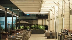Ampla área de estar interna com cadeiras e mesas de vime, um jardim vertical central e um espaço de bar com garrafas.