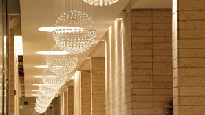 Um corredor com vários candelabros esféricos pendurados no teto, uma receção e uma área de estar com um sofá e cadeiras.