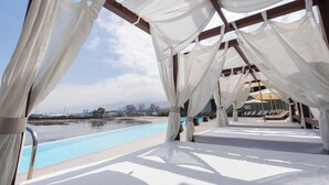 Uma área à beira da piscina com toldos brancos e cadeiras de descanso.