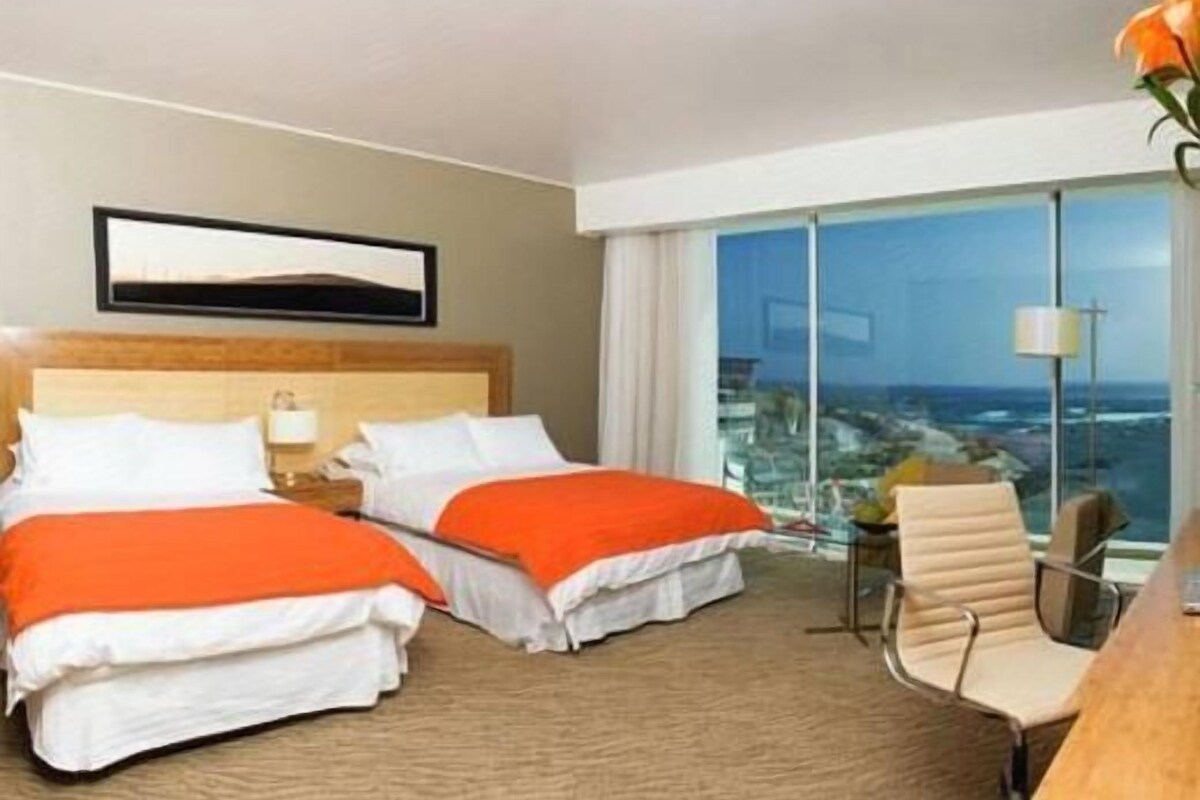 Quarto de hotel com duas camas, vista para a cidade e uma janela grande.
