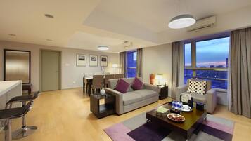 Quarto de hotel moderno com área de estar, espaço para refeições e uma grande janela com vista para a cidade.