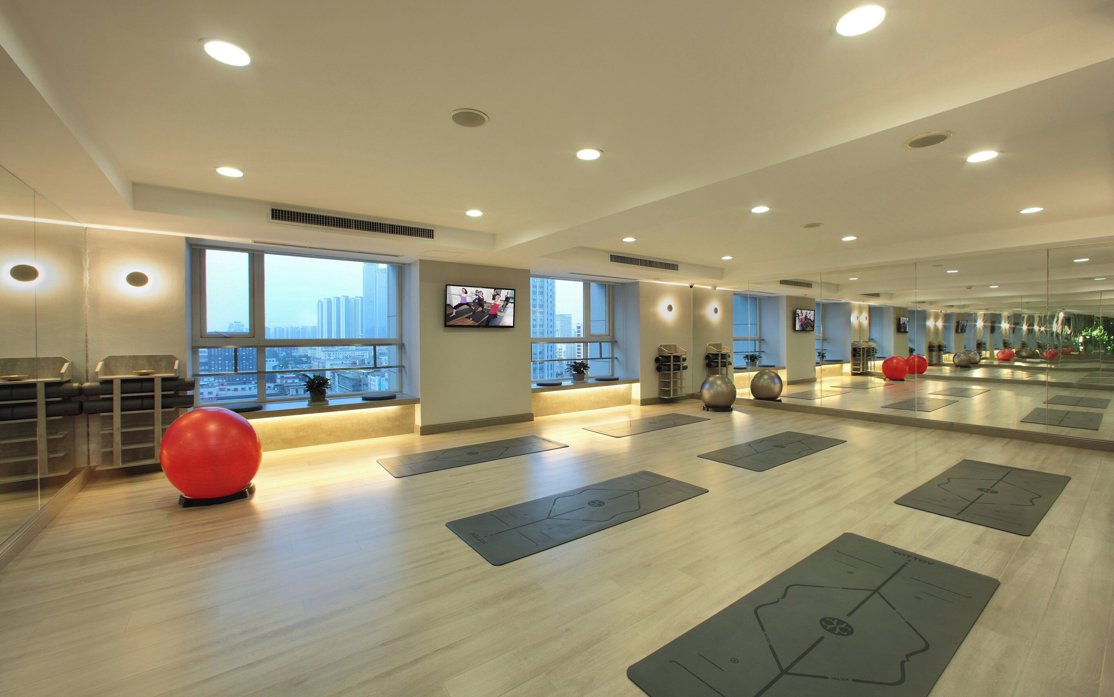 Uma academia espaçosa com colchonetes de exercício, grandes janelas e vista para a cidade.