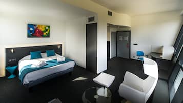 Quarto de hotel moderno com cama, escrivaninha, cadeira e um quadro na parede.