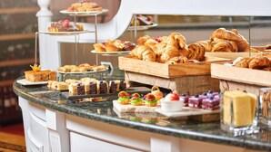 Buffet com diversos pastéis e sobremesas, incluindo croissants e tortas de fruta, disposto sobre um balcão de mármore.