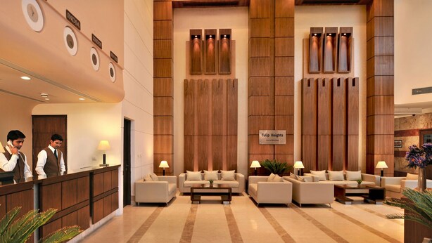 Um hall de hotel com uma mesa de recepção, várias áreas de estar e uma placa indicando 'Tulip Heights'.