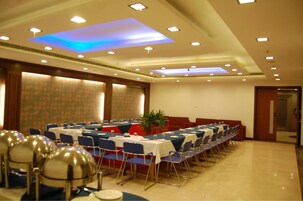 Uma sala de conferências com mesas, cadeiras, ilumina ção embutida e parede com padrão.