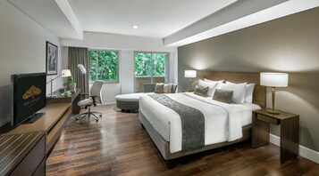 Quarto de hotel com uma cama grande, uma escrivaninha, uma cadeira e uma televisão.
