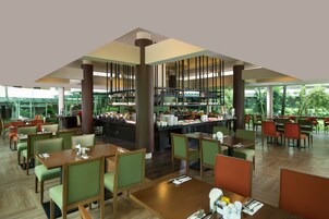 Um restaurante moderno com várias áreas de refeições, um bar central e grandes janelas com vista para o exterior.