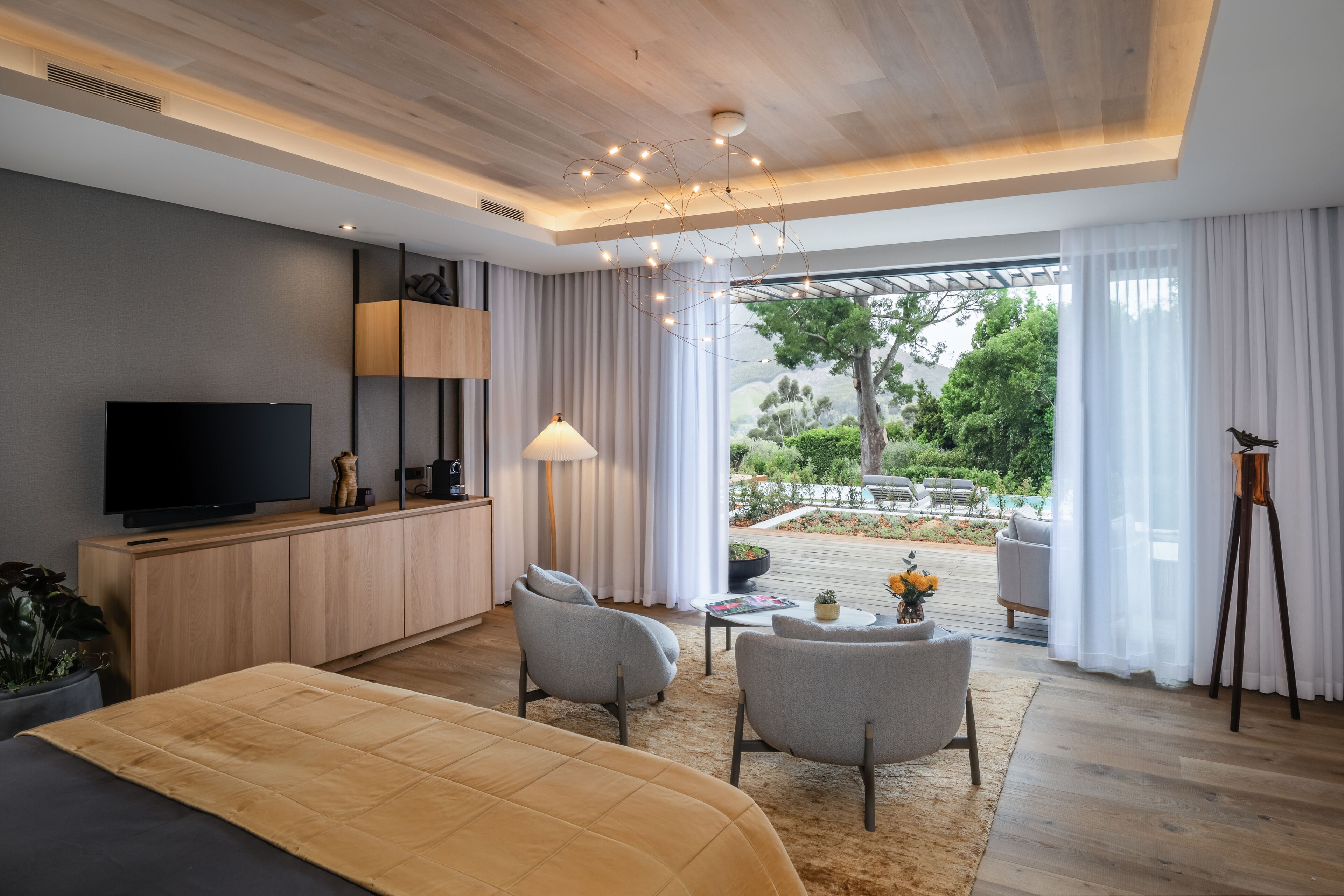 Quarto moderno com uma cama grande, uma televisão, uma escrivaninha e vista para o exterior.